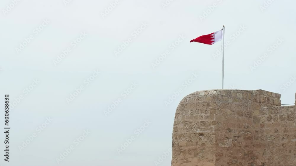 Flag of Bahrain Qalat fortress at sky background in Manama waving ...