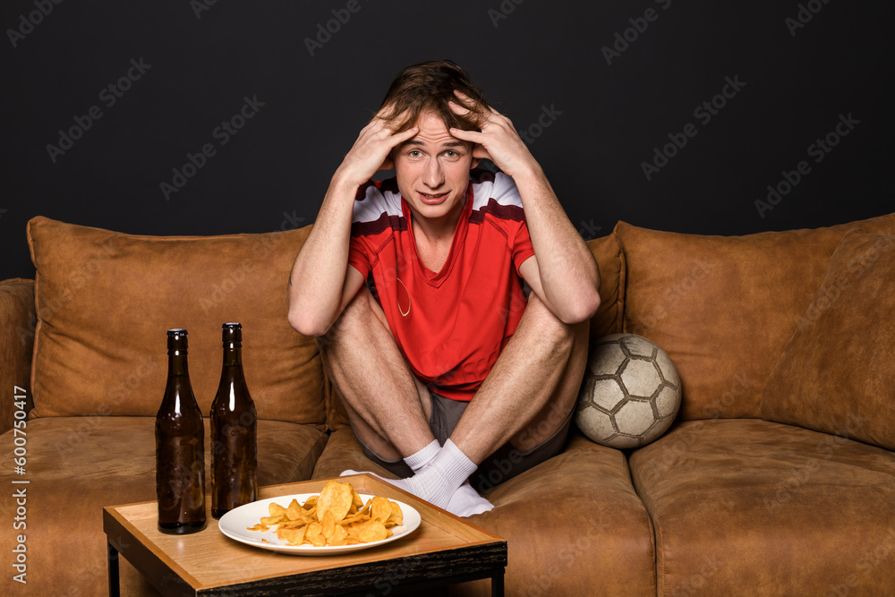 An upset and stressed football fan in a red jersey is watching a match ...