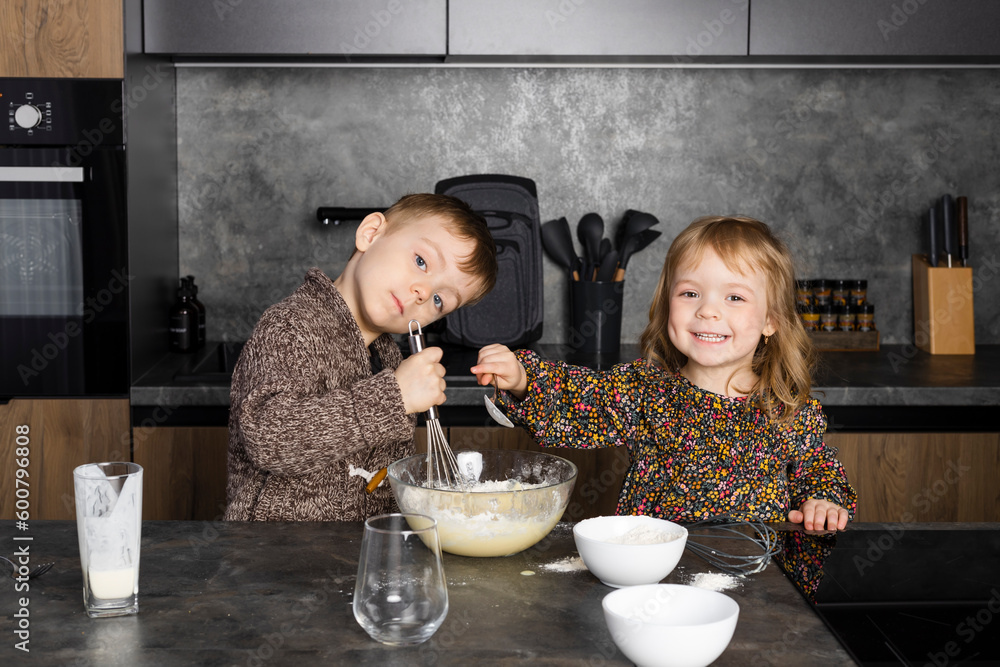 Little siblings cooking together on a modern kitchen, helping each ...
