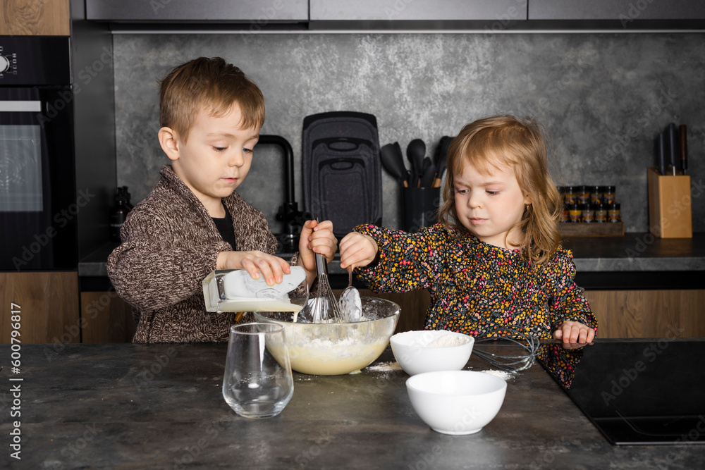 Little siblings cooking together on a modern kitchen, helping each ...