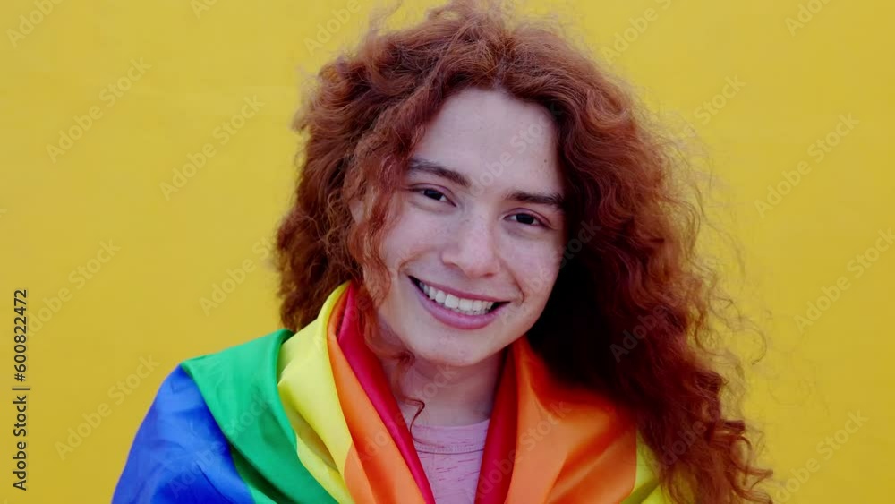 Portrait of red haired non binary man with rainbow flag smiling at ...