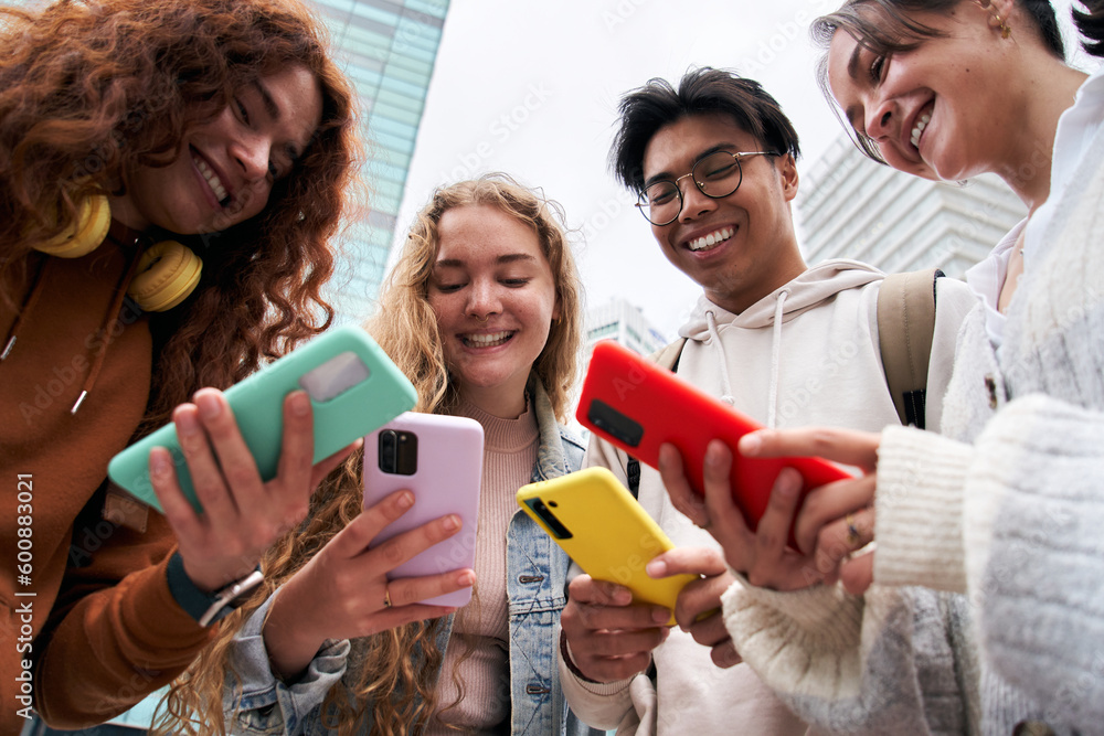 Portrait of four smiling friends looking at cell phone from below ...