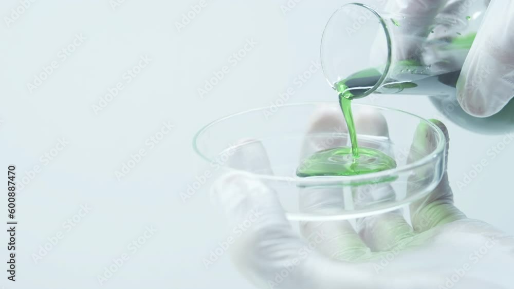 Green liquid in a laboratory flask and petri dish. Hands in white ...