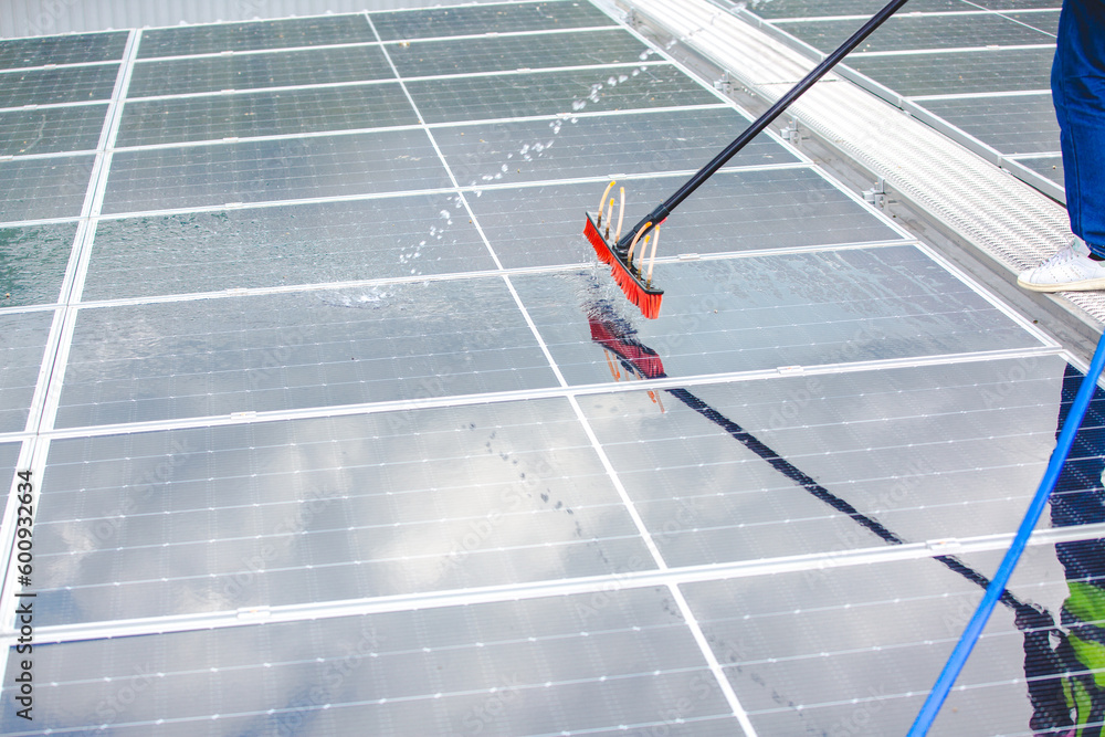Professional worker cleaning solar panels with brush and washing with ...