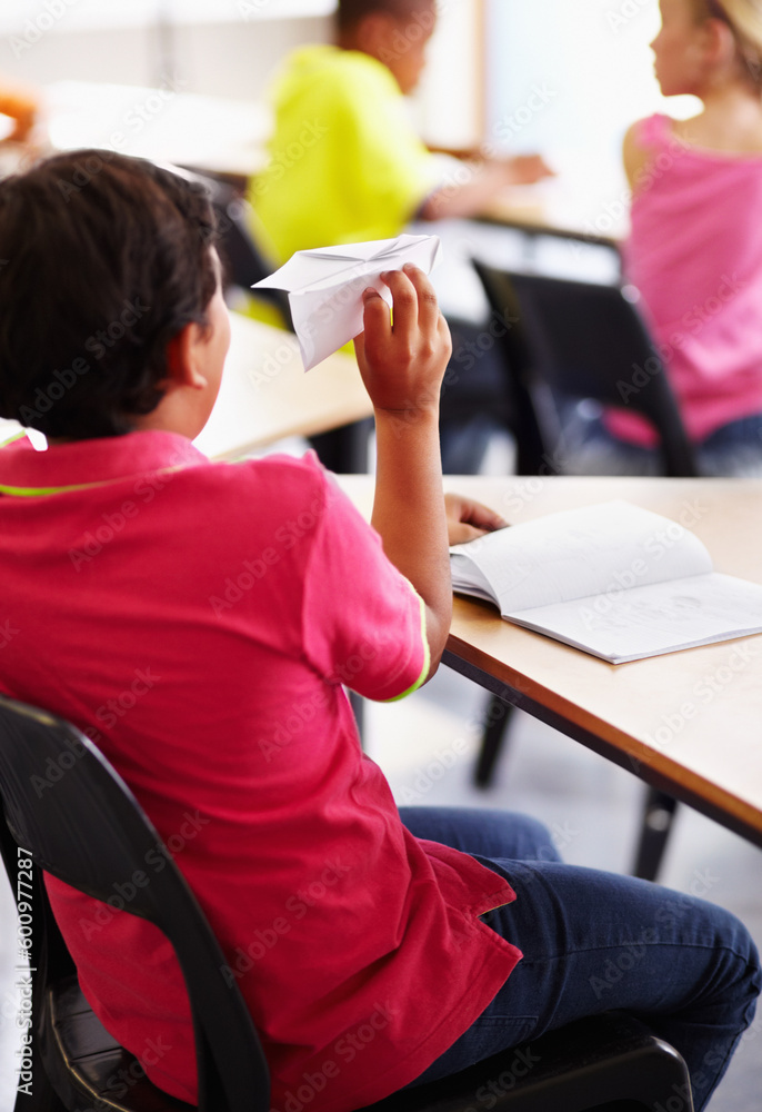 Bully, boy child with paper plane in classroom and sitting at his desk with behavior problem ...
