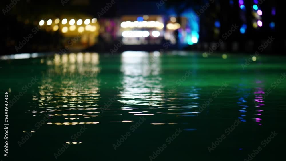Long outdoor swimming pool at night, bright lights seen blurred on ...