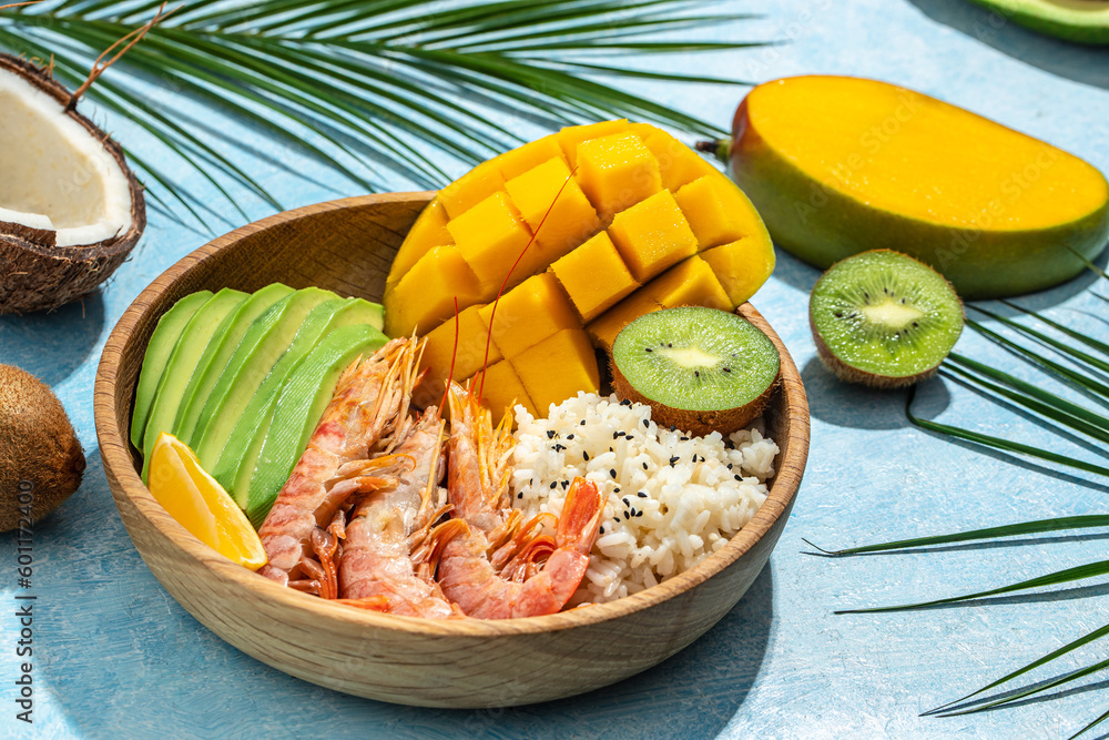 tropical bowl with avocado, prawns, rice, mango, kiwi and coconut, tropical food on the sea ...