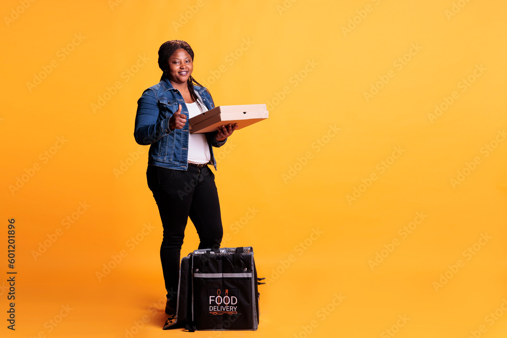 Confident deliverywoman holding pizza cartboard box while doing thumb ...