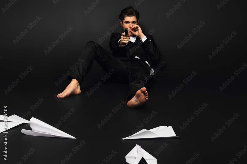 Young mafia member with a slicked back hair, in black suit, smokes a ...