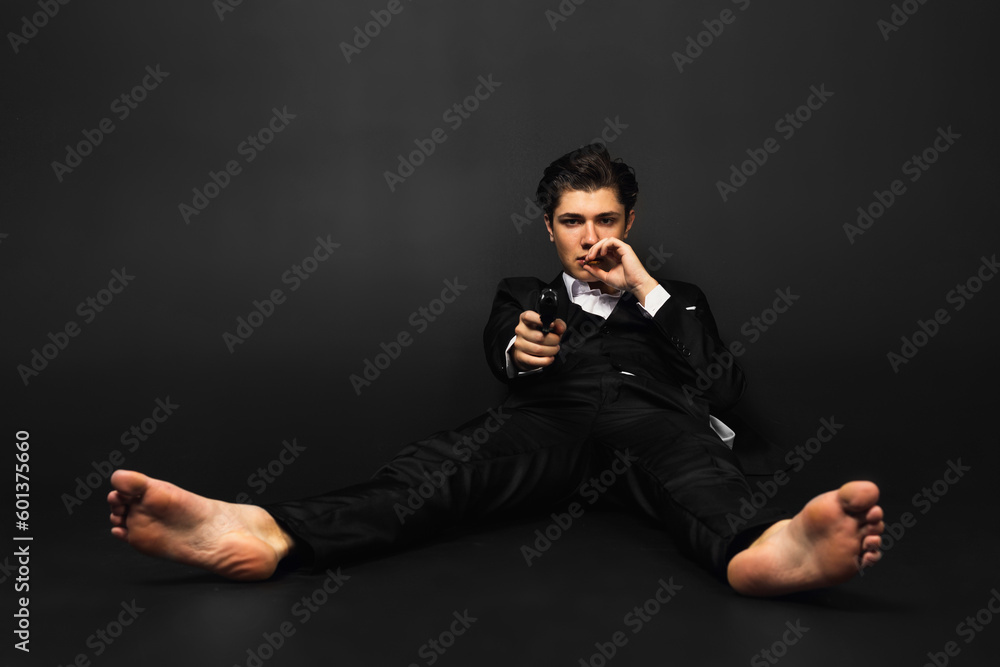 Young mafia member with a slicked back hair, in black suit, smokes a ...