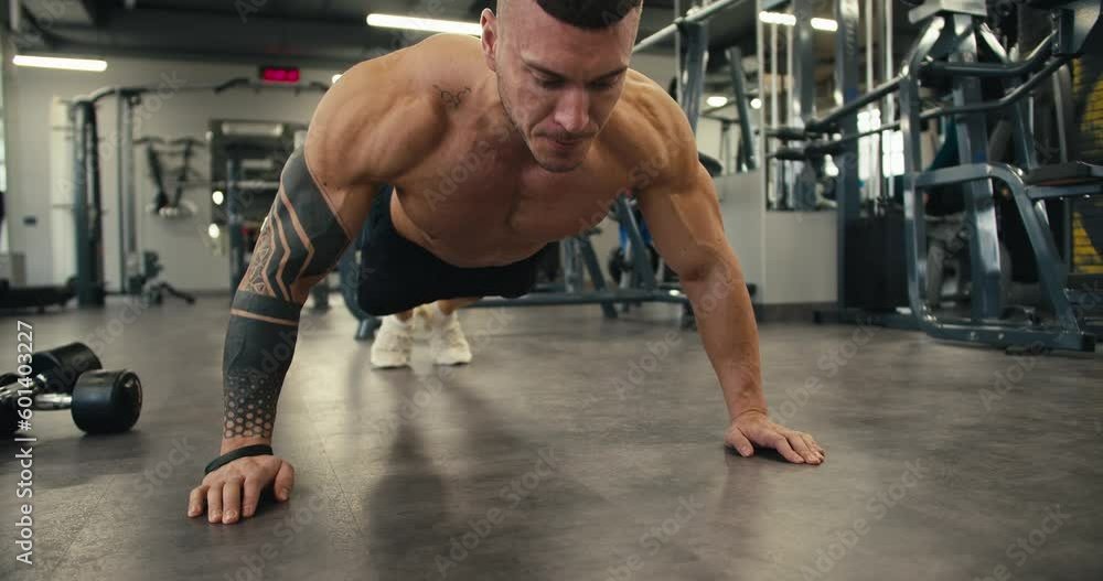 Strong athletic man trains shirtless in the gym, doing push-ups. Lean ...
