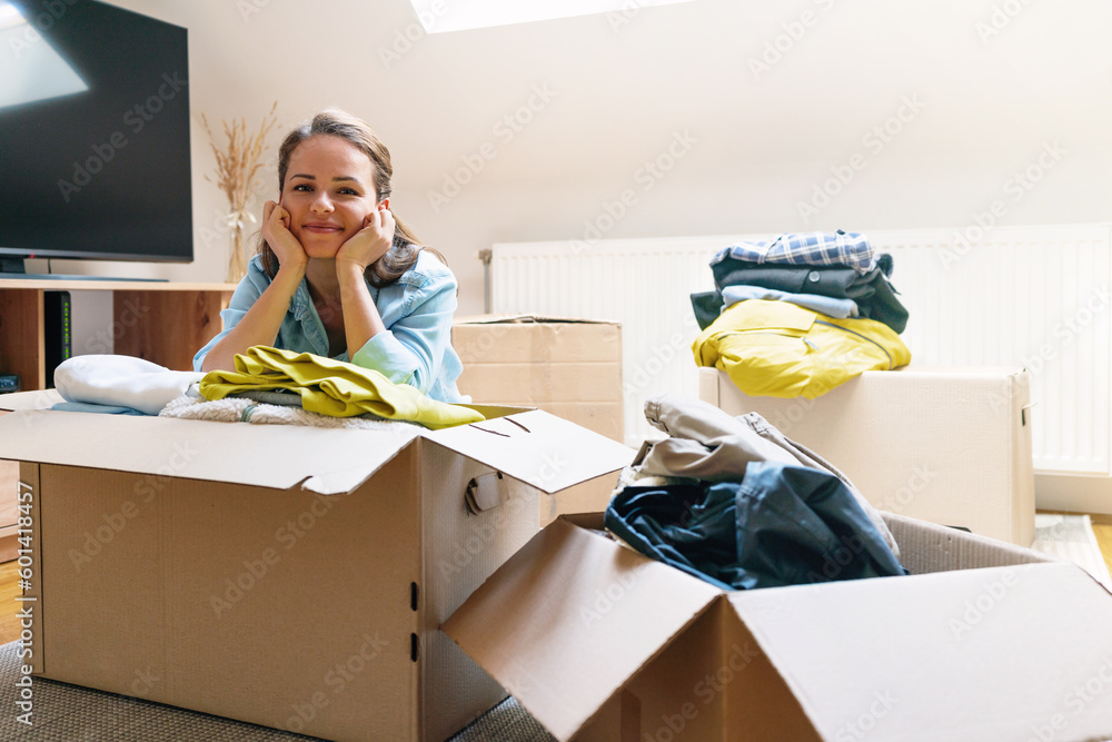 Young brunette woman packing her clothes in cardboard boxes at home ...