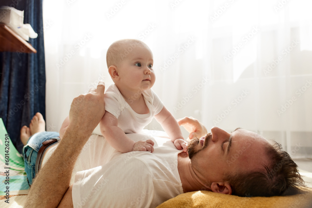 Happy dad holds his newborn baby in his arms while lying on the floor ...