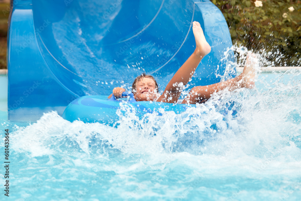 Joyful boy in swimming goggles slides down the blue water slide on an ...