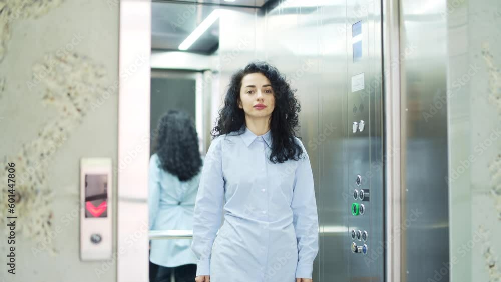A confident woman exits an elevator in a modern office building or ...