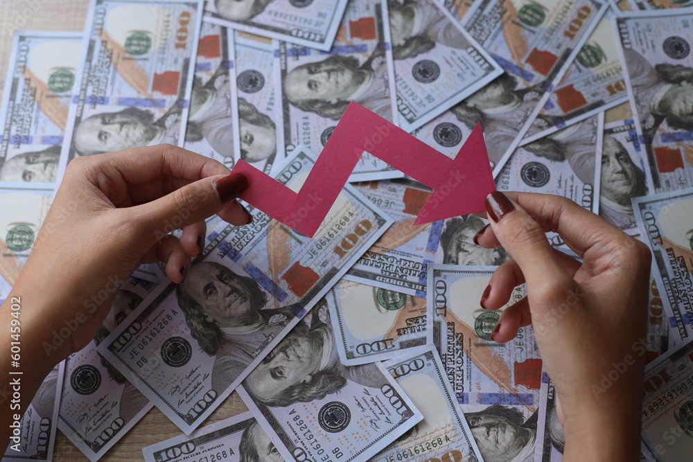 Hand holding red arrow going downwards on dollar bills background ...