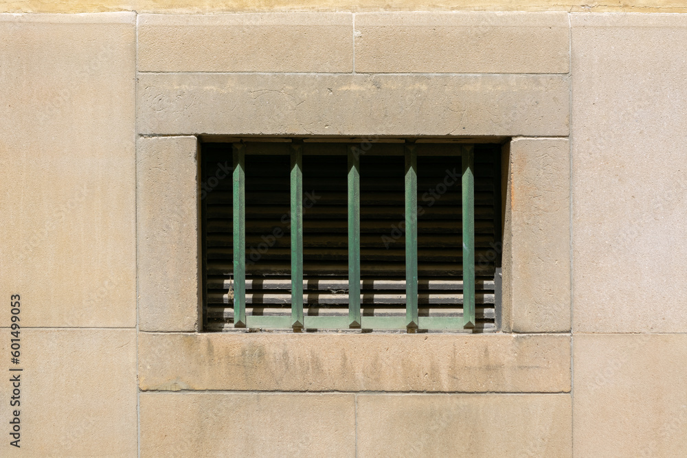 Small rectangular window on a stone wall, covered with green metal bars ...