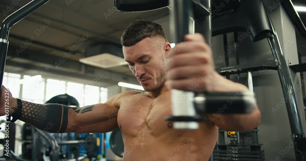 A focused athlete flexes his arm muscles on the exercise machine ...
