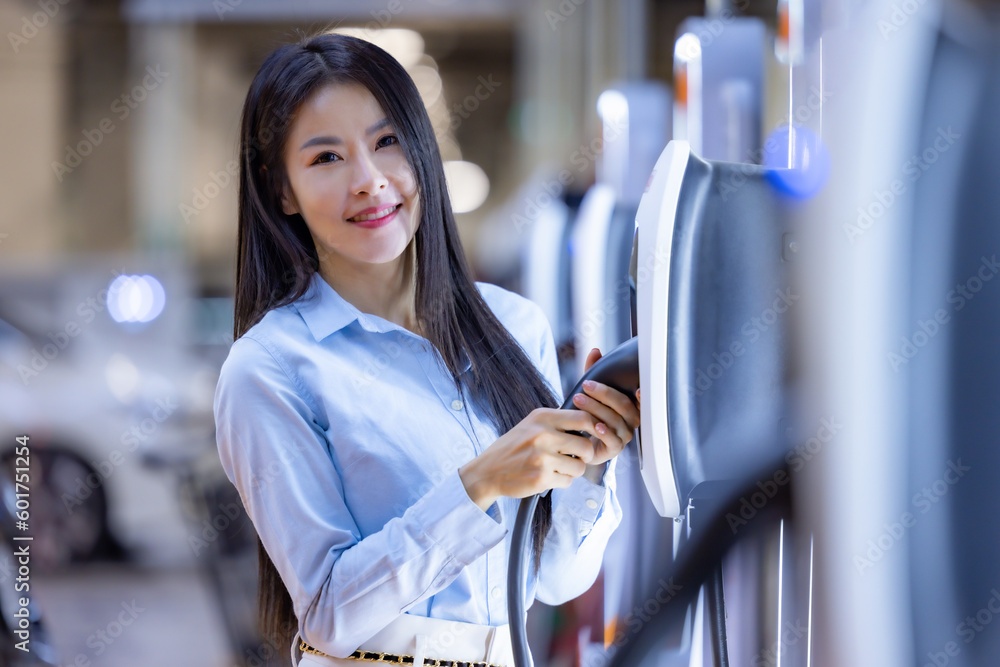Young Asian woman holding the CCS 2 EV charging connector at EV charging station in department ...