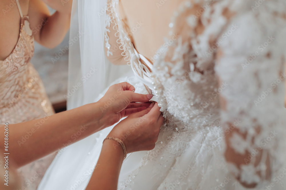 The bride's friends fasten the white voluminous dress of the bride ...