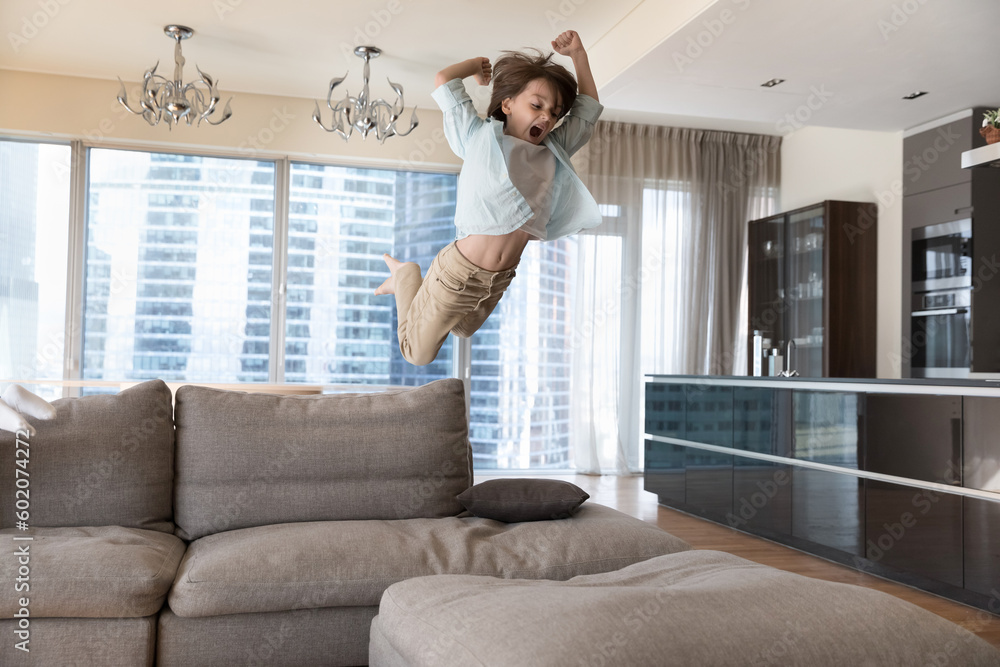 Excited crazy boy kid jumping on big sofa, throwing body on soft couch ...
