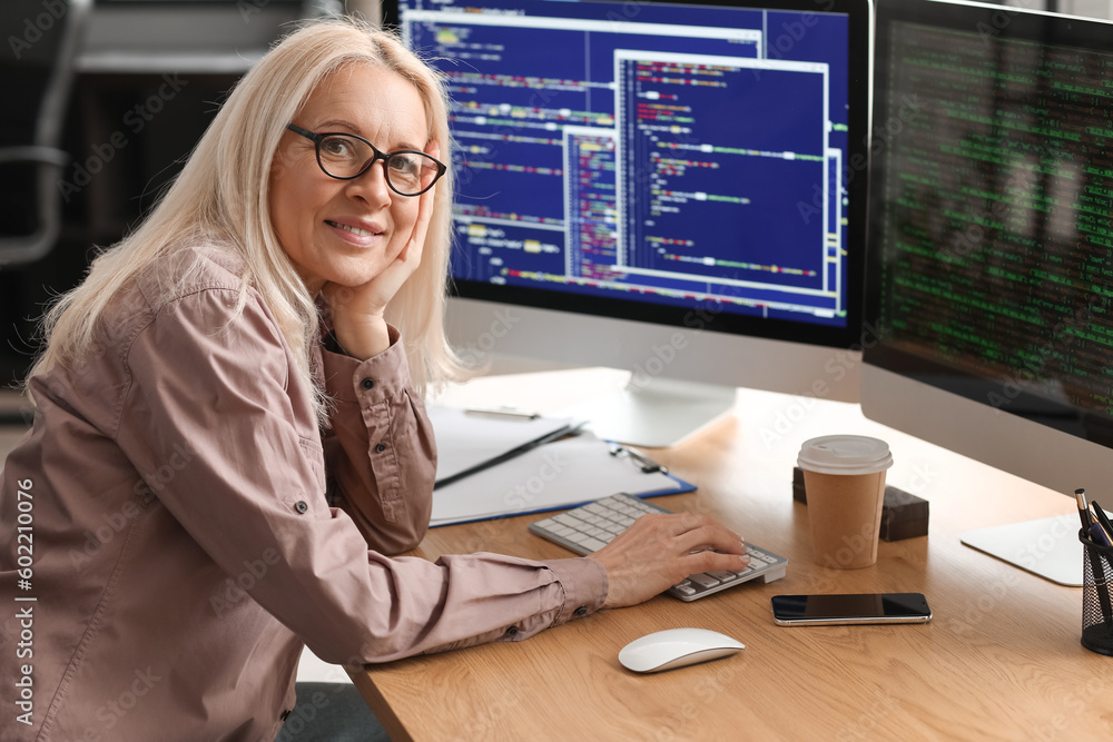 Mature female programmer working with computer at table in office Stock Photo | Adobe Stock