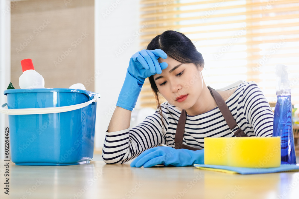 tired woman cleaner in apron and gloves for cleaning sitting with ...