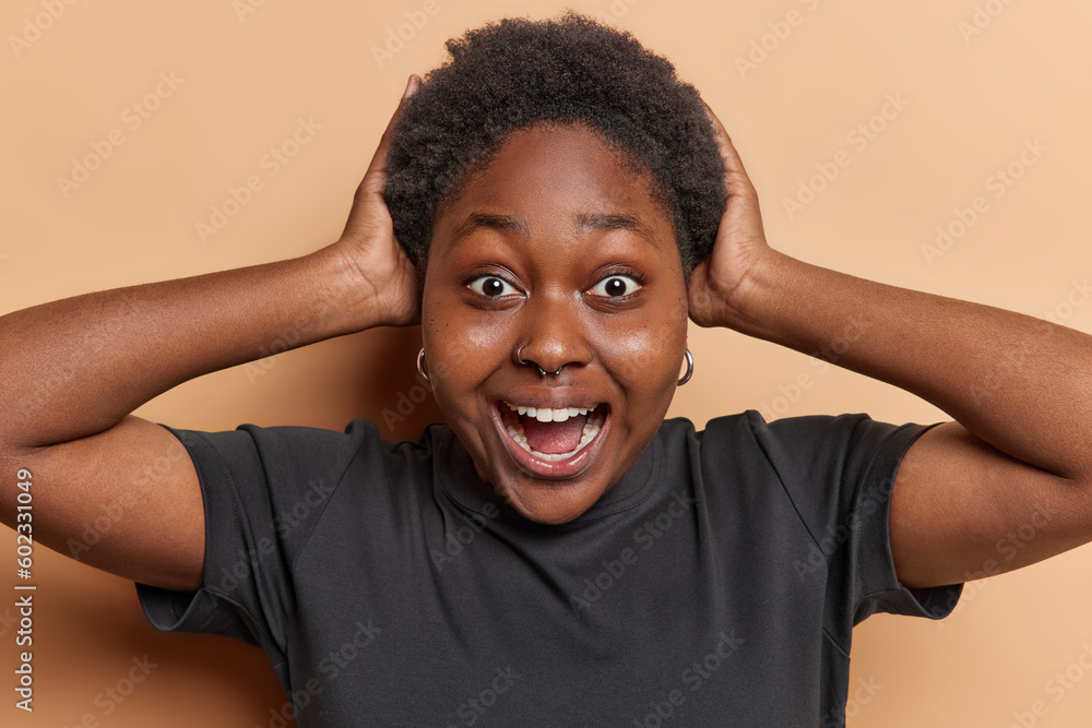 Shocked impressed dark skinned plump woman keeps hands on head stares ...