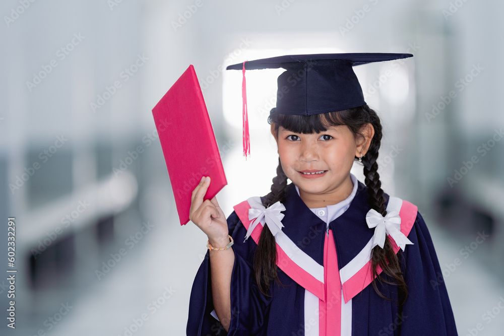 A cheerful kid graduate wearing an academic gown and graduation cap ...