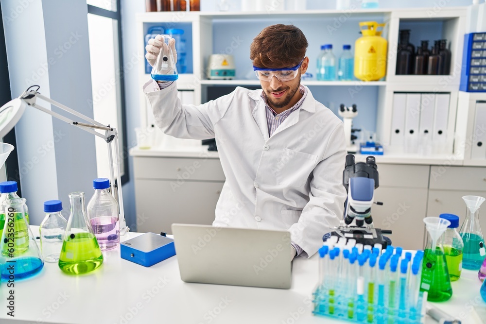 Young arab man scientist using laptop measuring liquid at laboratory ...