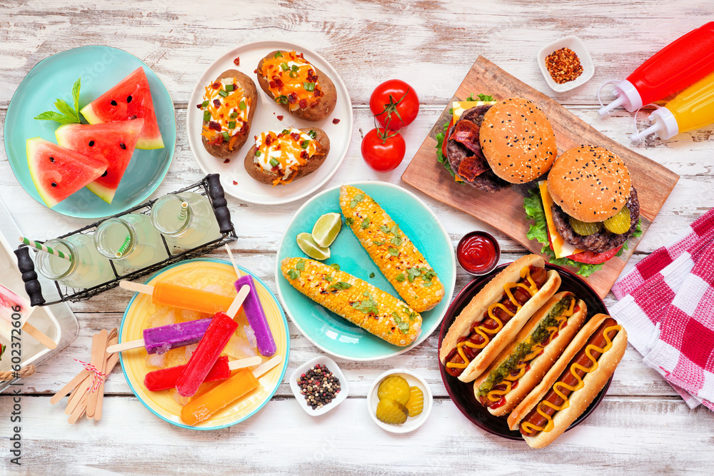 Summer BBQ food table scene. Hamburgers, hot dogs, potatoes, corn and ...