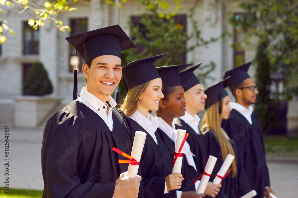 Happy graduate students dressed in black graduation gowns holding ...