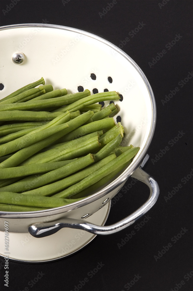 Kitchen collander filled with green beans brightly lit on isolated ...