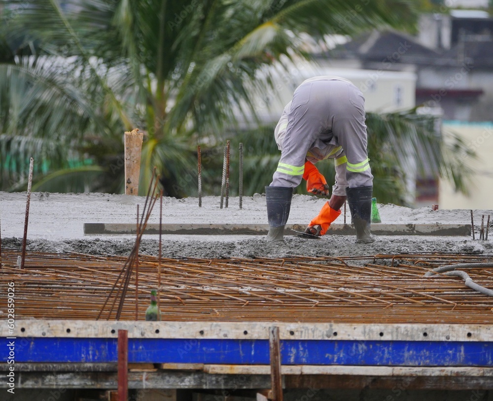 Construction site worker levelling and smoothing fresh cement on cast ...