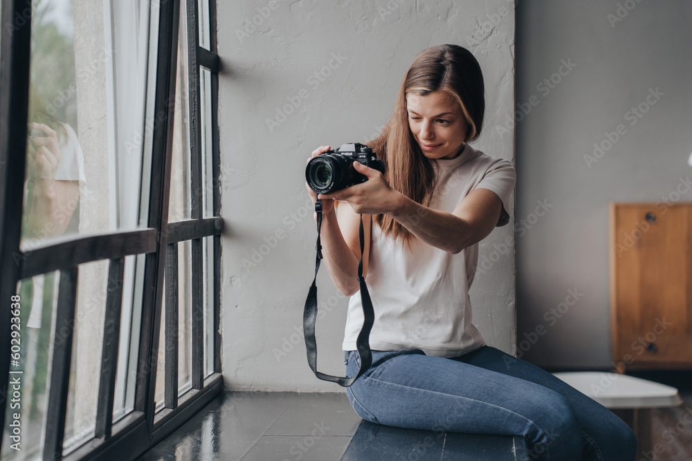 Young female photographer sitting on windowsill makes shoot trough ...