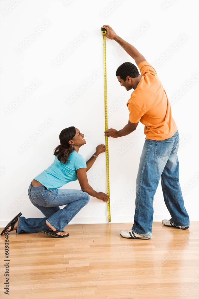 African American male and female measuring wall. Stock Photo | Adobe Stock