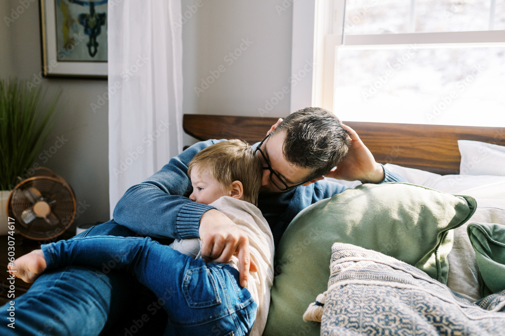 young dad hugging and holding his son while they lay in bed at home ...