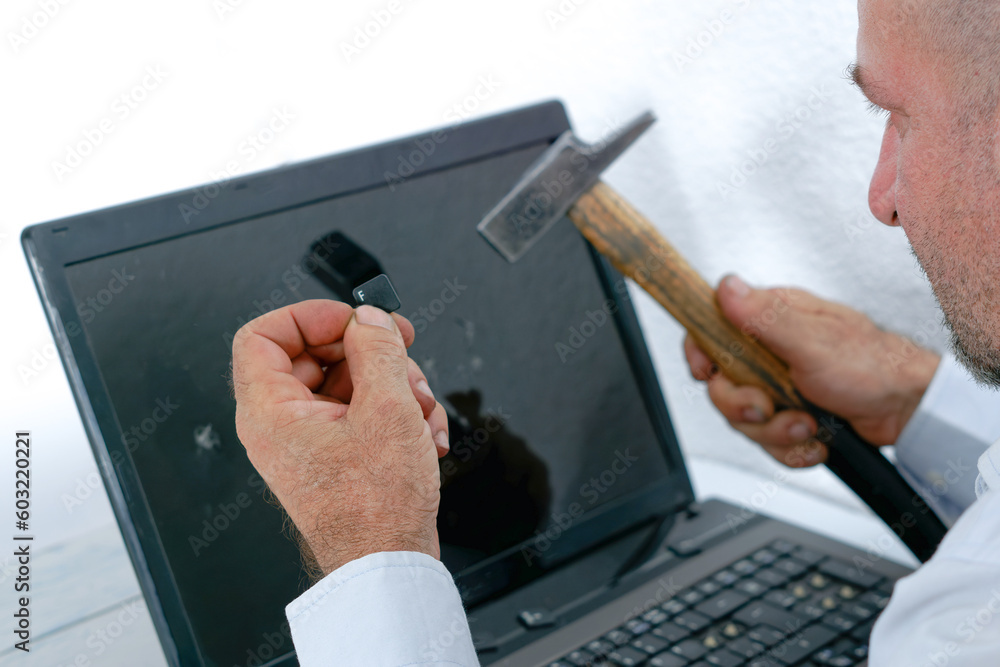 angry man seen in profile breaking a laptop with a hammer , white ...
