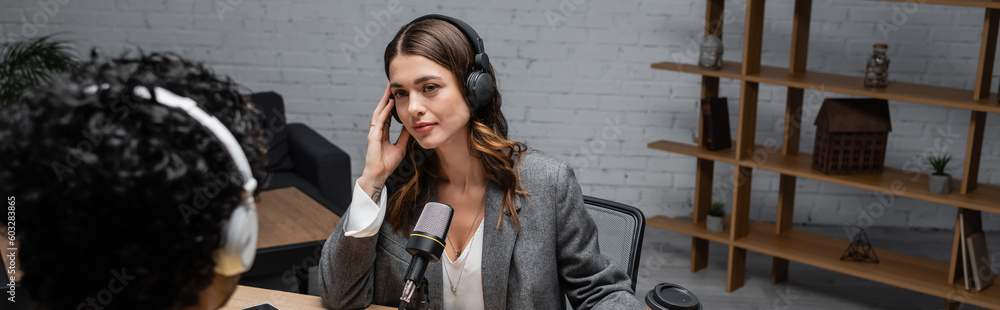 brunette radio host in grey blazer adjusting headphones during ...