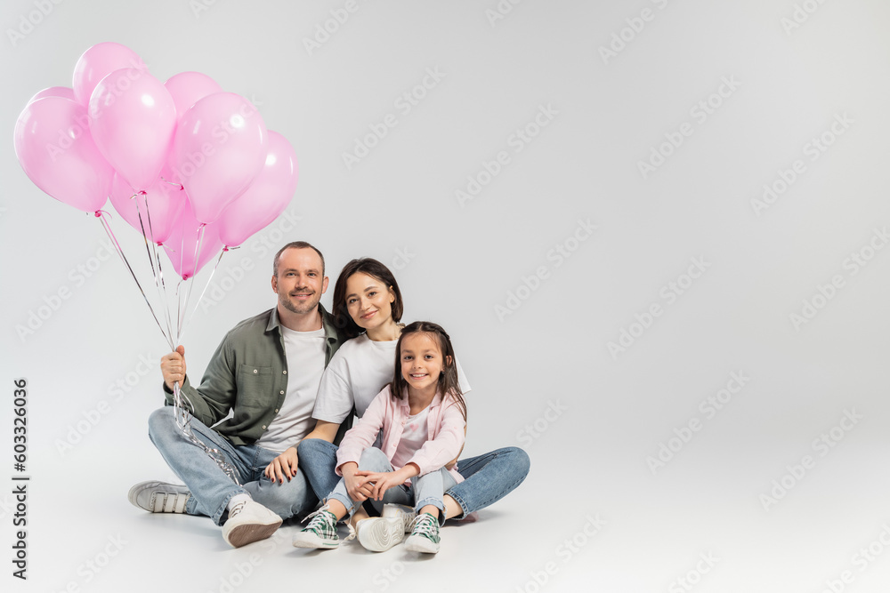 Smiling parents in casual clothes hugging preteen daughter and holding ...