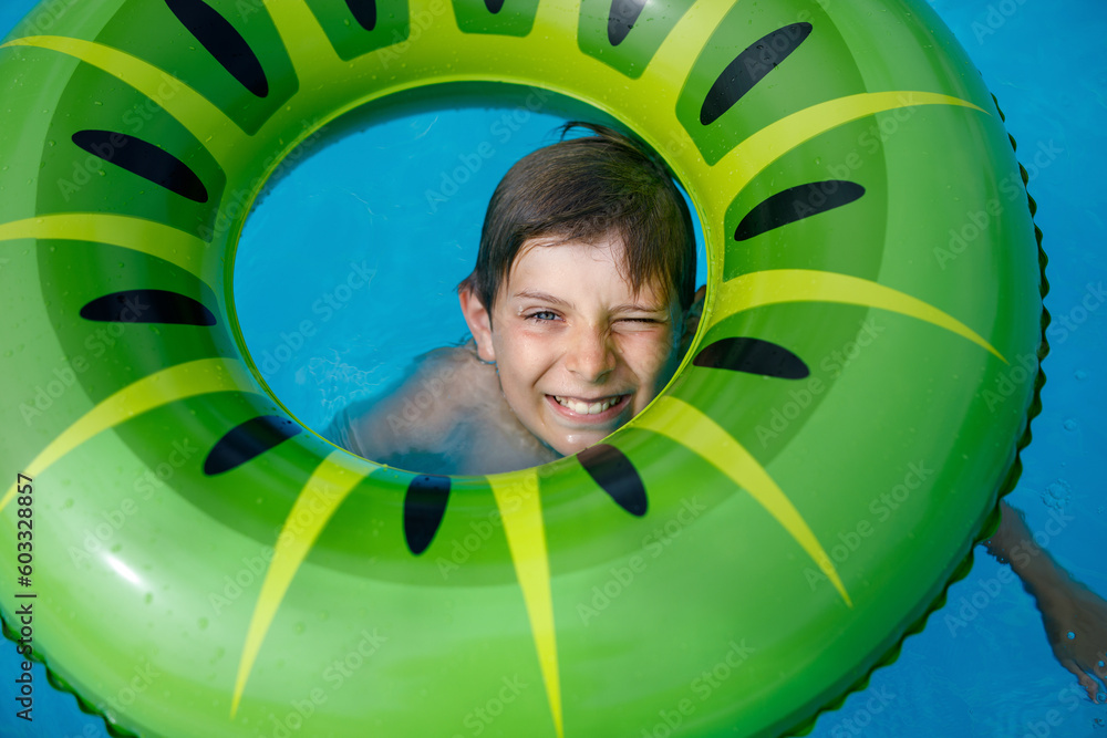 Cool school boy having fun on inflatable rubber circle in outdoor pool ...