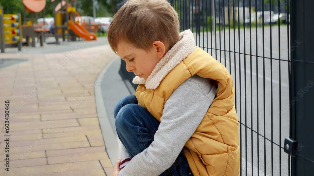 Portrait of little boy crying while sitting alone next to metal fence ...