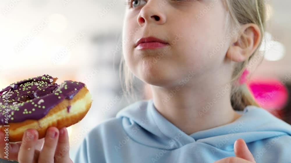 Little girl eats a donut in a cafe. Pretty girl eating a donut while ...