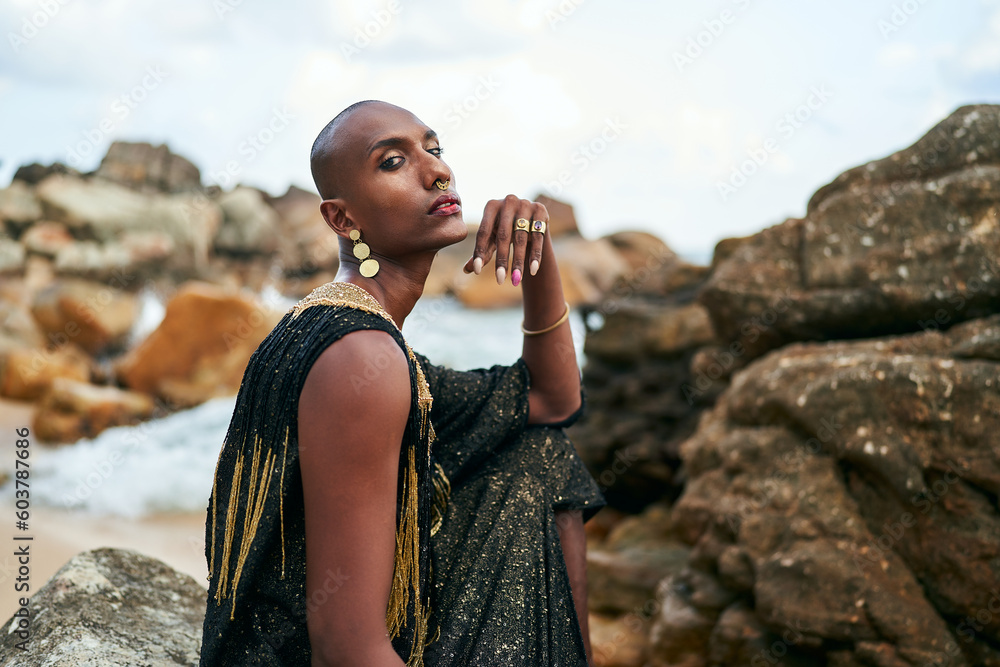 Non-binary black person in luxury dress on rocks in ocean. Trans ethnic fashion model wearing ...