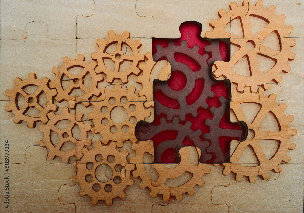 Cog wheels coming out from underneath a jigsaw puzzle. solving the ...