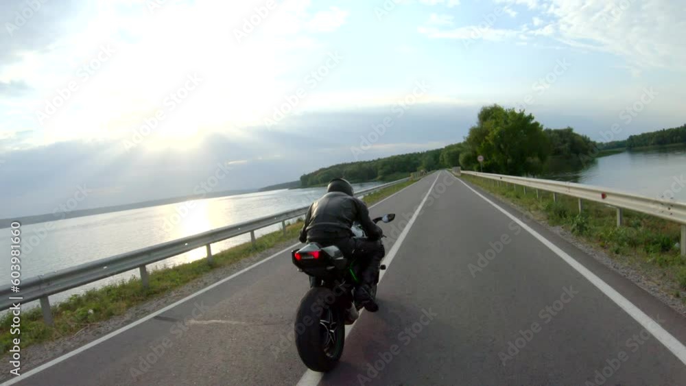 Biker riding on modern sport motorbike through road near lake ...