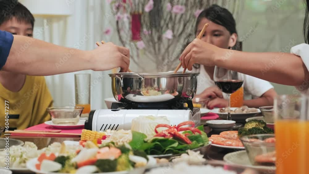 Mother and dad using chopsticks for putting food ingredients in hot pot ...