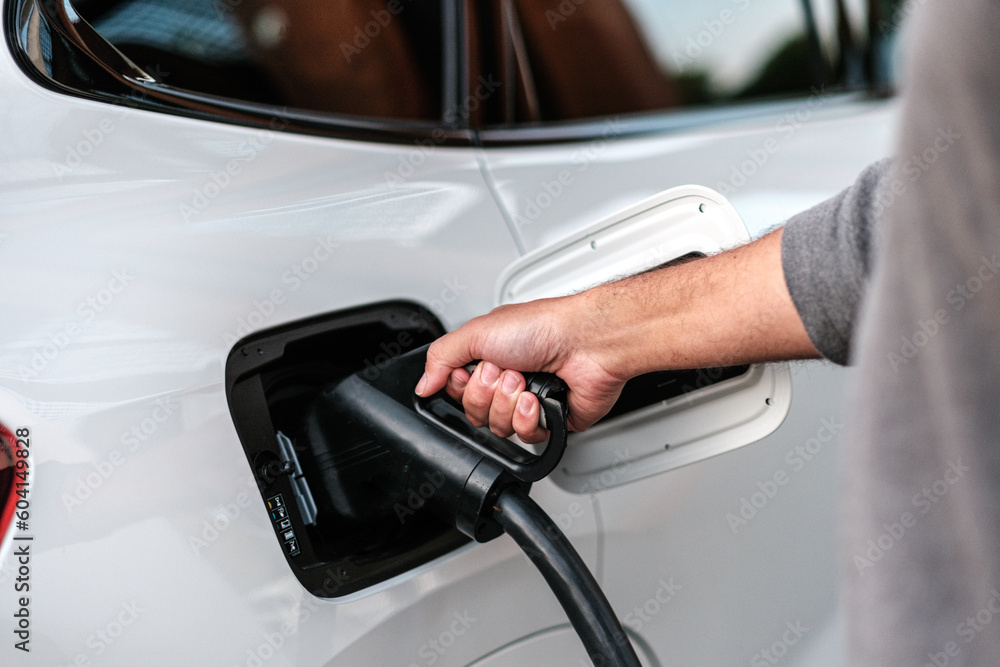 Foto de Person plugging in a charging cable to a white car at a ...