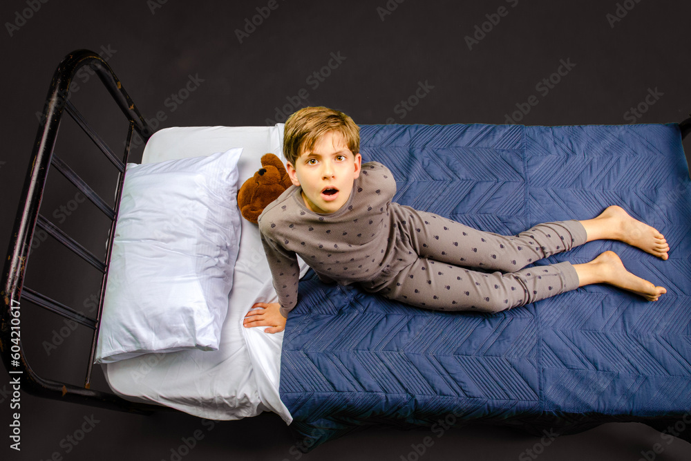 Startled young boy sitting up in bed looking upward in fear at ...