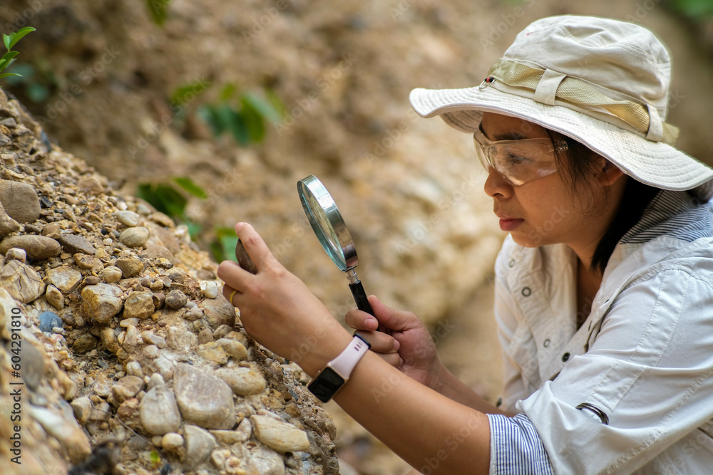 Female geologist using magnifying glass to examine and analyze rock ...